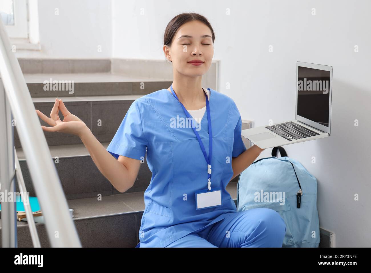 Asian medical intern with laptop meditating on stairs at university ...