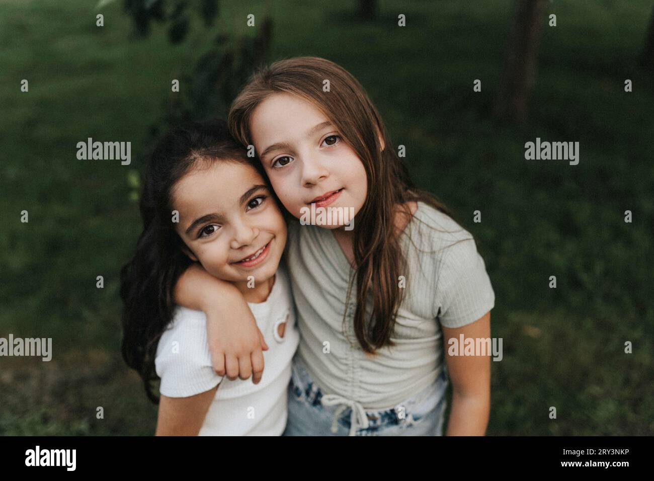 Portrait of smiling sisters standing with arm around at park Stock ...