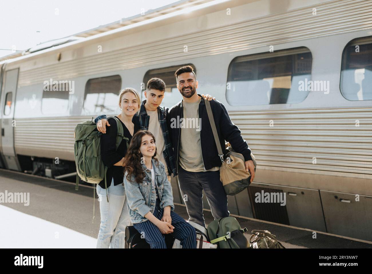 Portrait of smiling family standing with luggage in front of train at ...