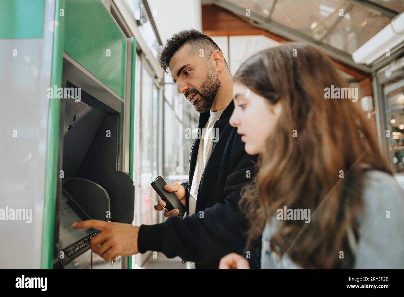 Father using ATM machine while standing with daughter at railroad ...