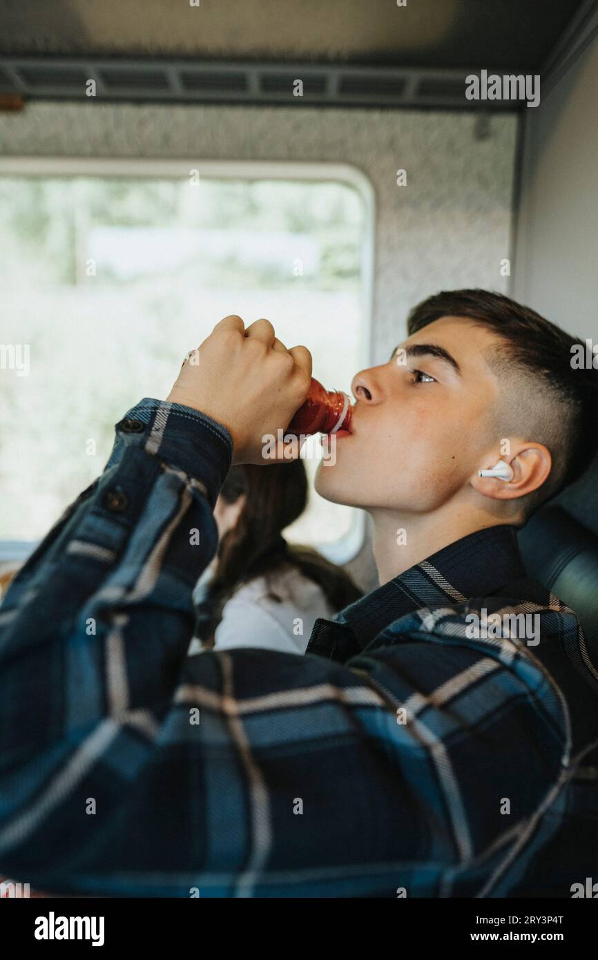Side view of boy drinking juice from bottle in train Stock Photo - Alamy