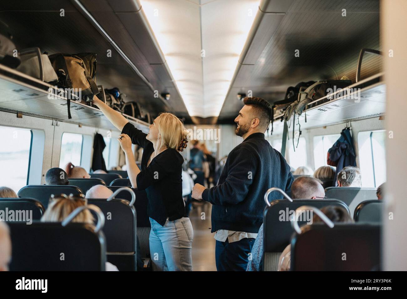 Woman helping man to load luggage on shelf in train Stock Photo - Alamy