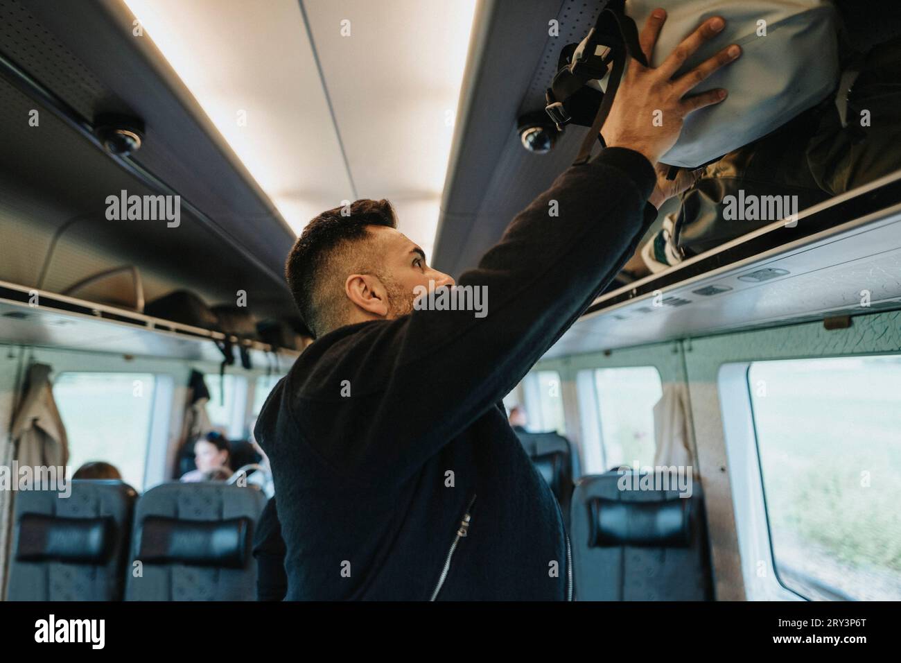 Side view of man loading luggage on shelf in train Stock Photo - Alamy