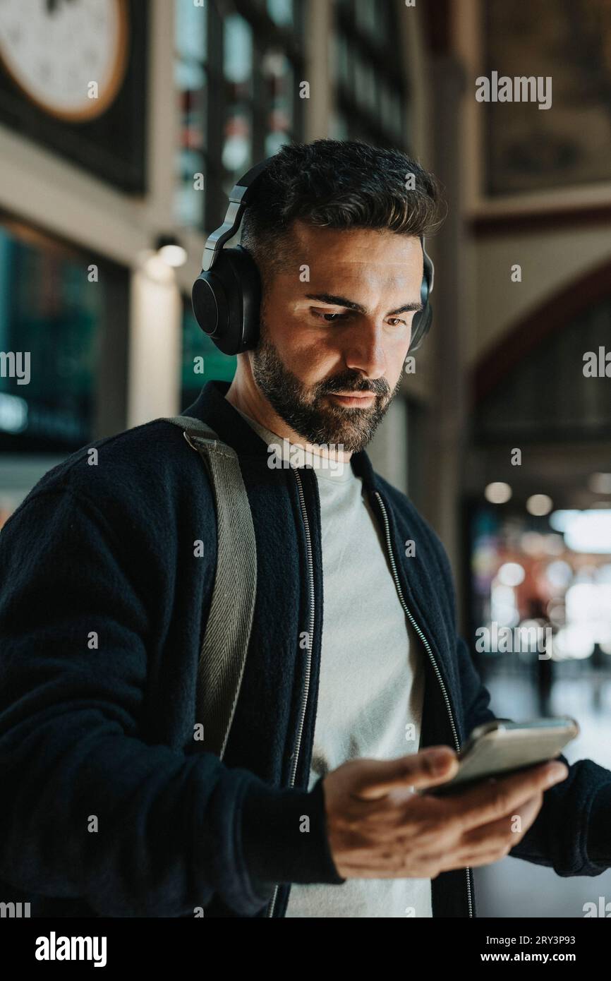 Man wearing bluetooth headphones holding smart phone at station Stock ...