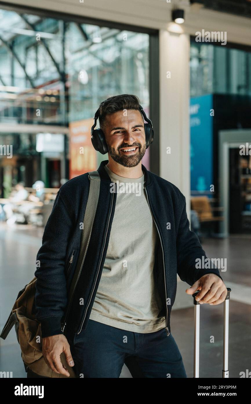 Portrait of happy man wearing bluetooth headphones while standing with ...