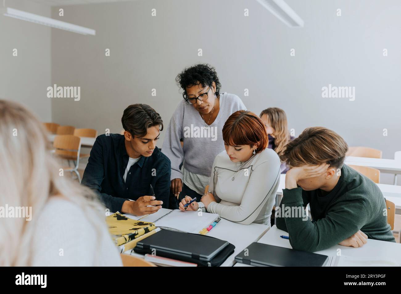 Teacher standing behind students studying at desk in classroom Stock ...