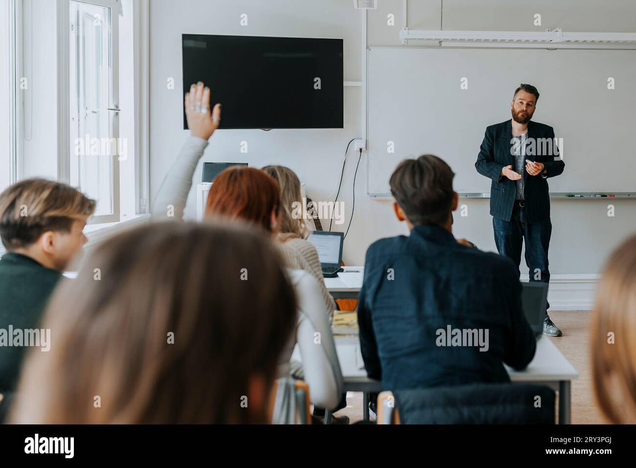 Male professor teaching while female student sitting with hand raised ...