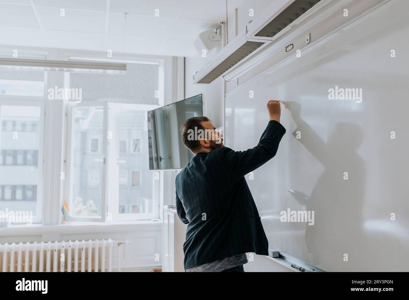 Side view of mature male professor writing on whiteboard in classroom ...
