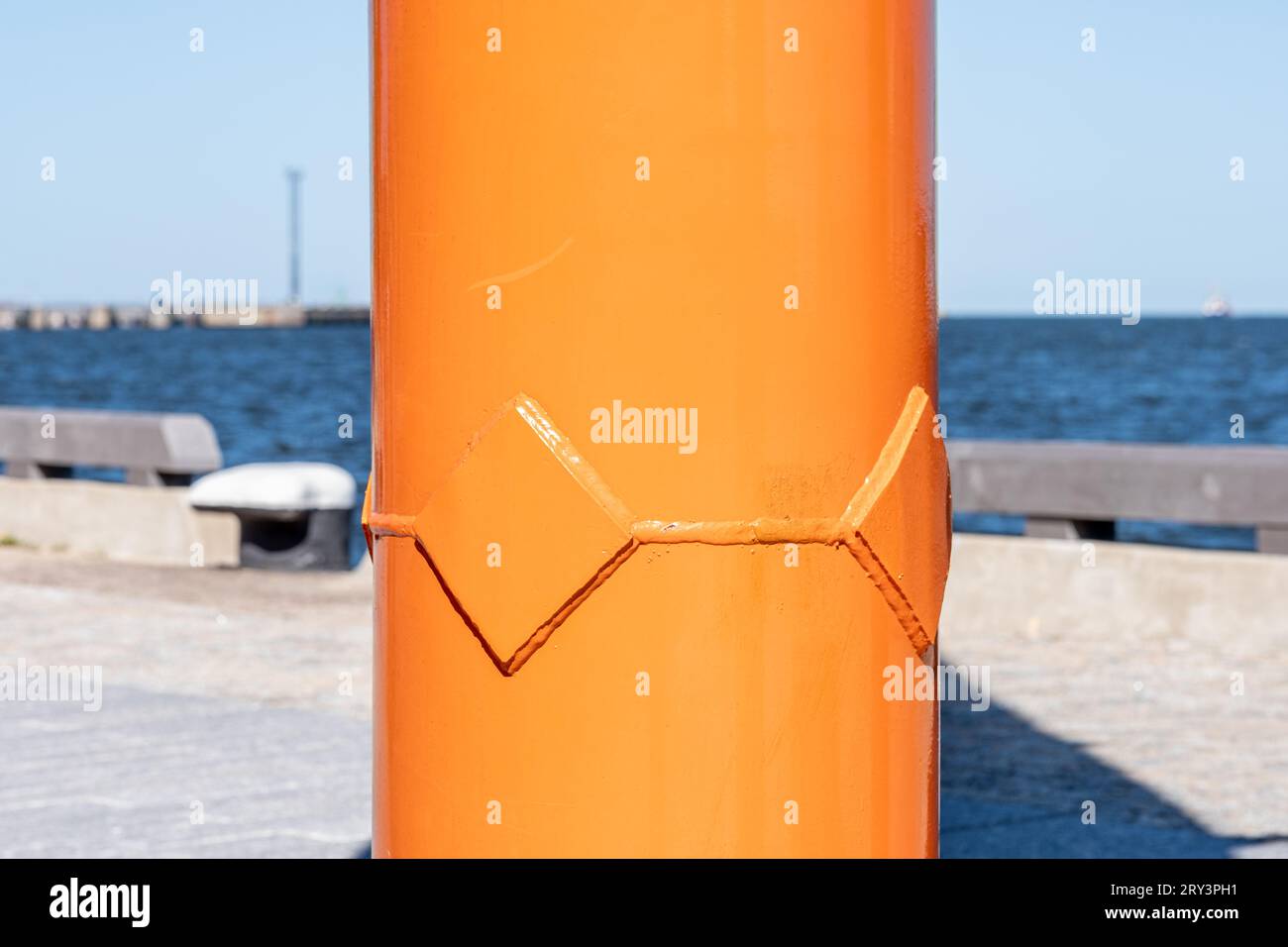 A huge metal bright orange tube on the seashore. In the background, a ...