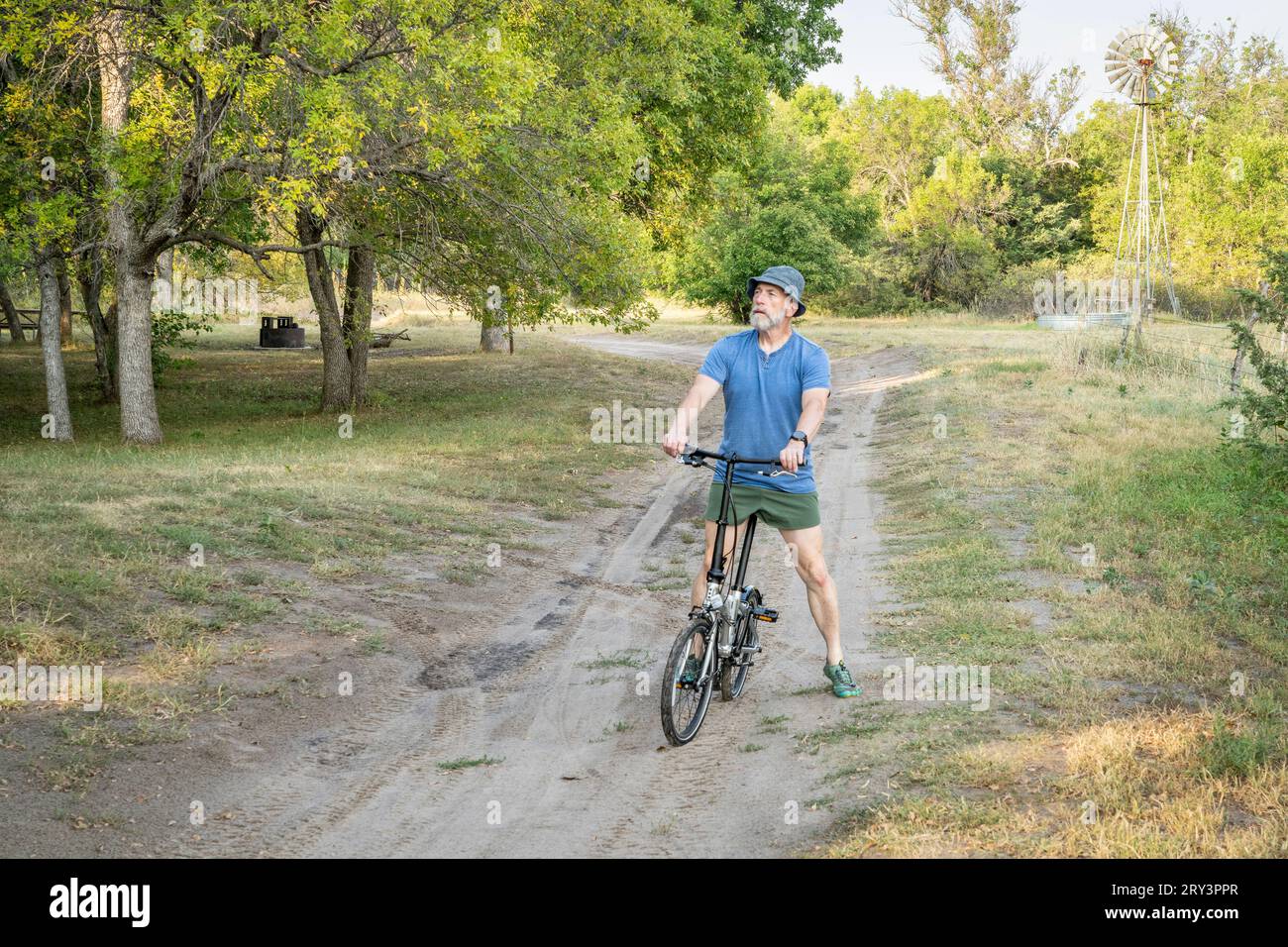athletic senior man is riding a folding bike on a sandy road in Whitetail Campground in Nebraska ...