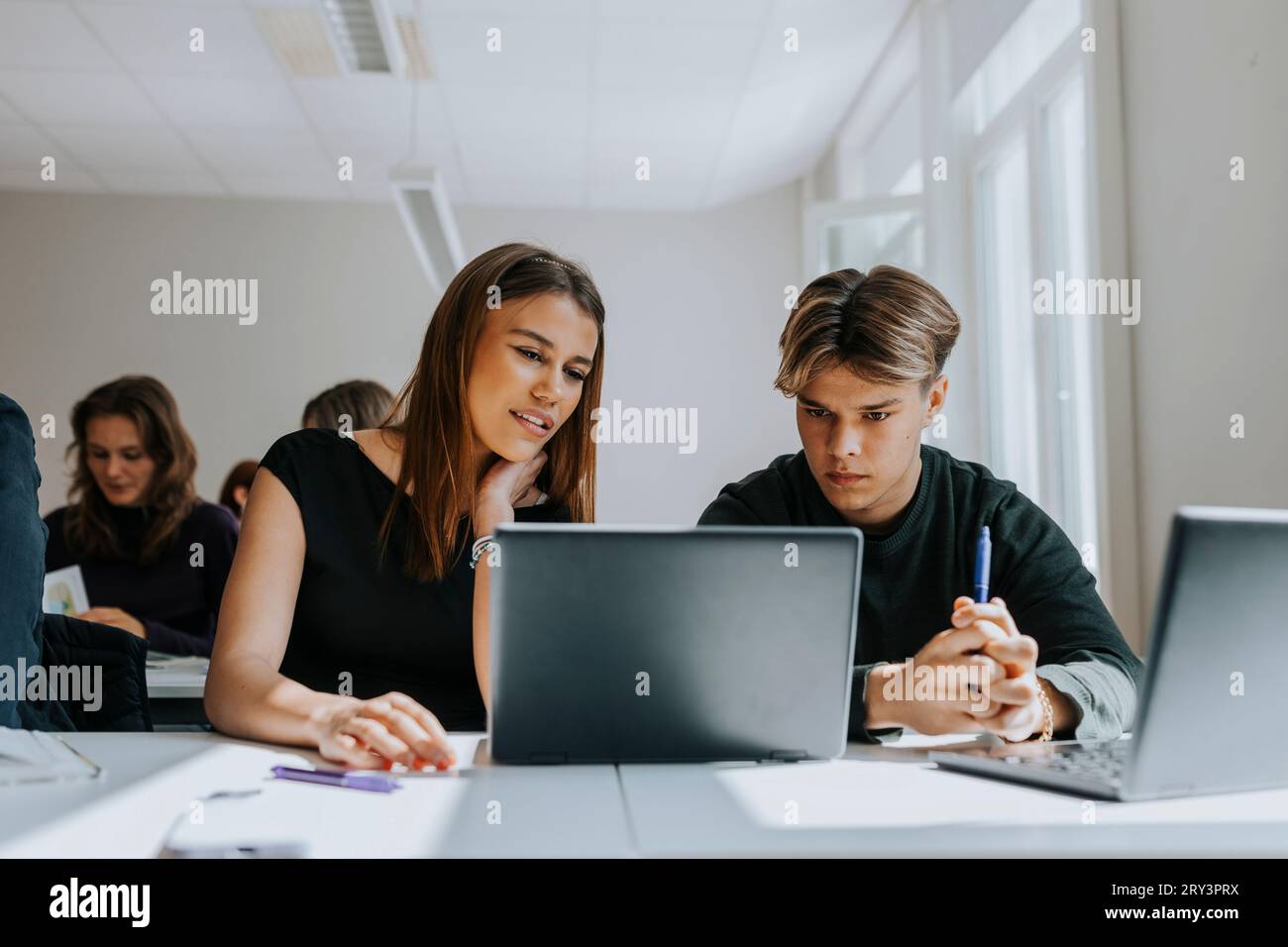 Multiracial male and female students sharing laptop at desk in ...