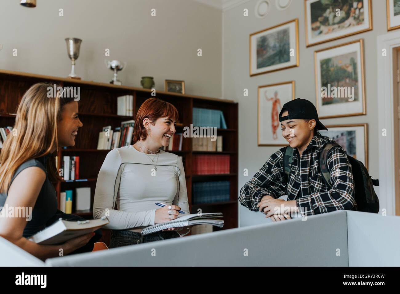 Happy male and female students talking against bookshelf in library ...