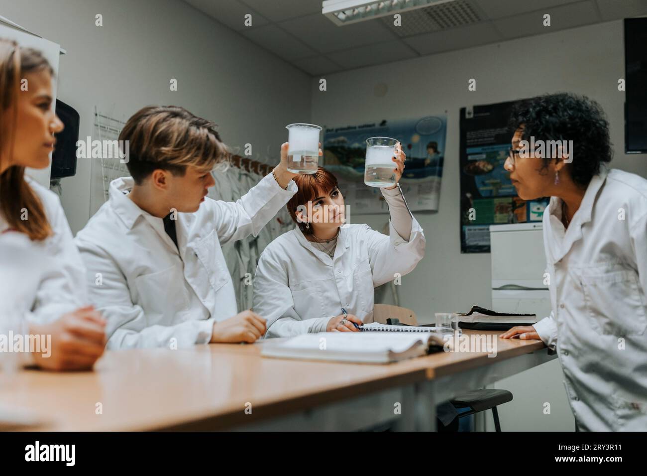Teacher and students examining chemical in beaker at school laboratory ...