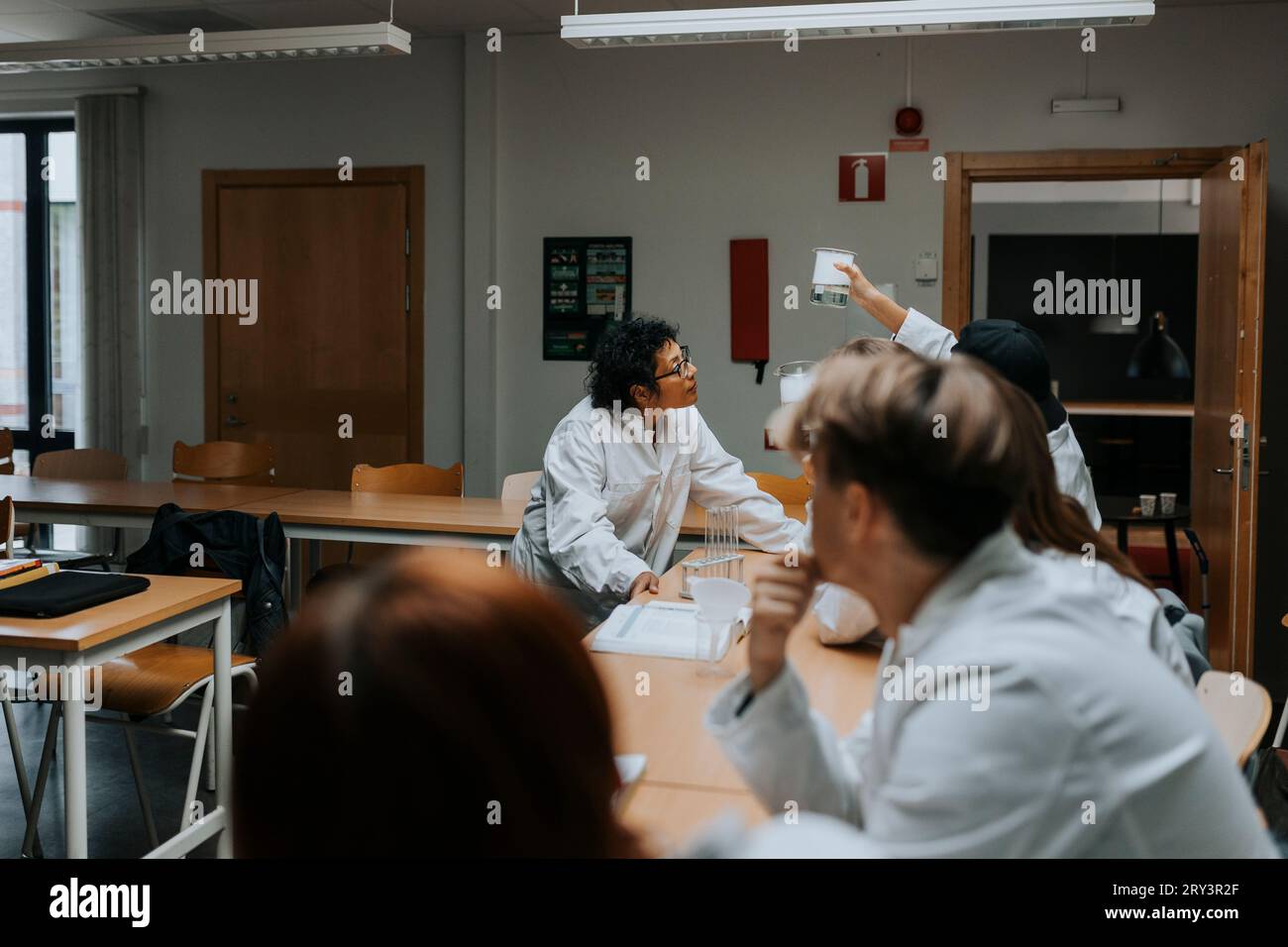 Teacher examining chemical in beaker with students at laboratory Stock Photo - Alamy