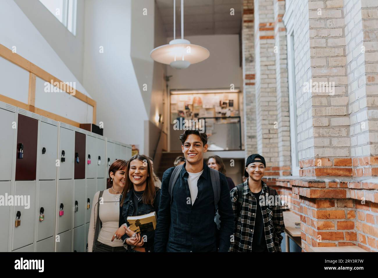 Happy male and female students walking by locker in school corridor ...