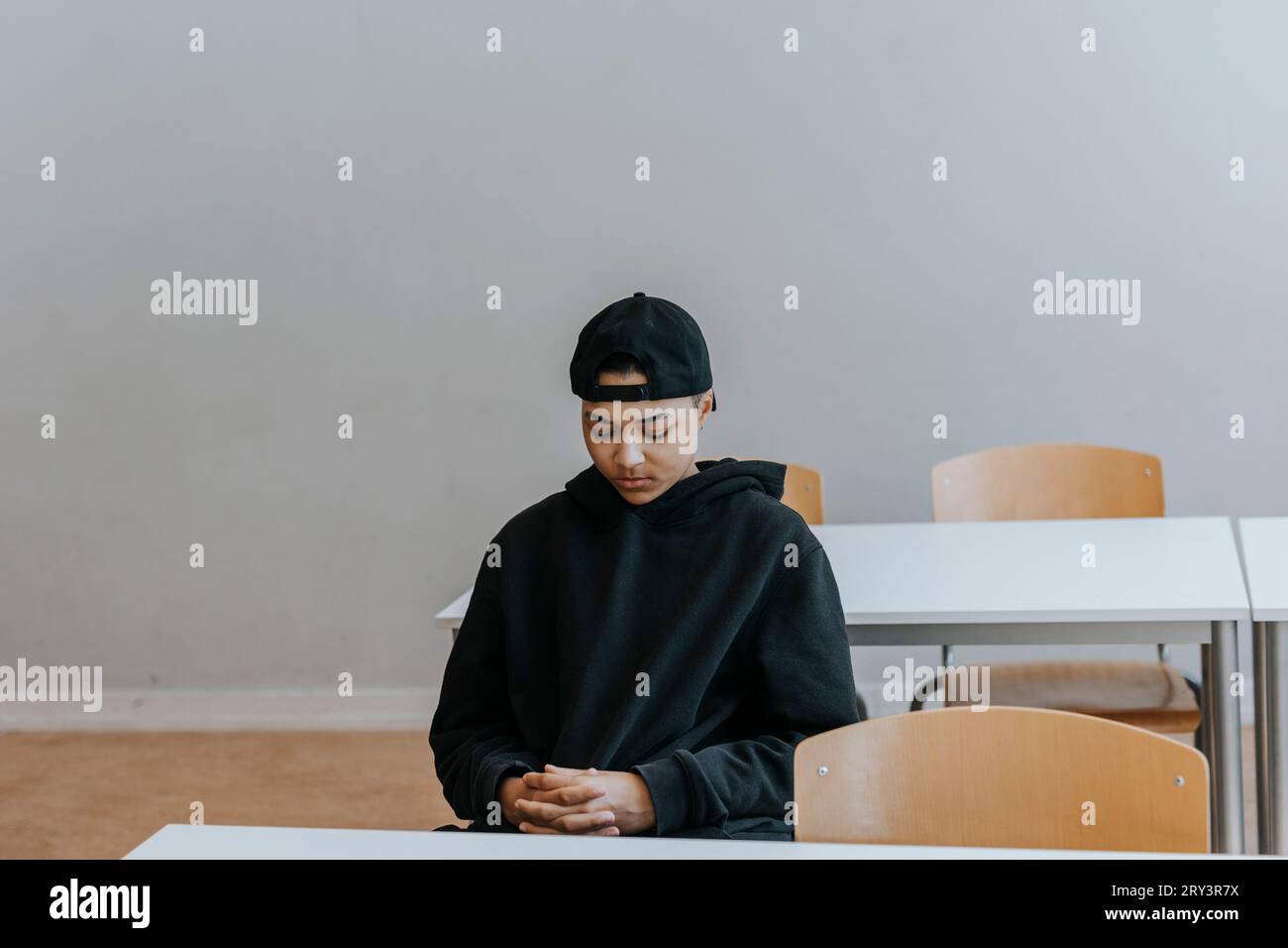 Sad young male student sitting with hands clasped in classroom Stock ...