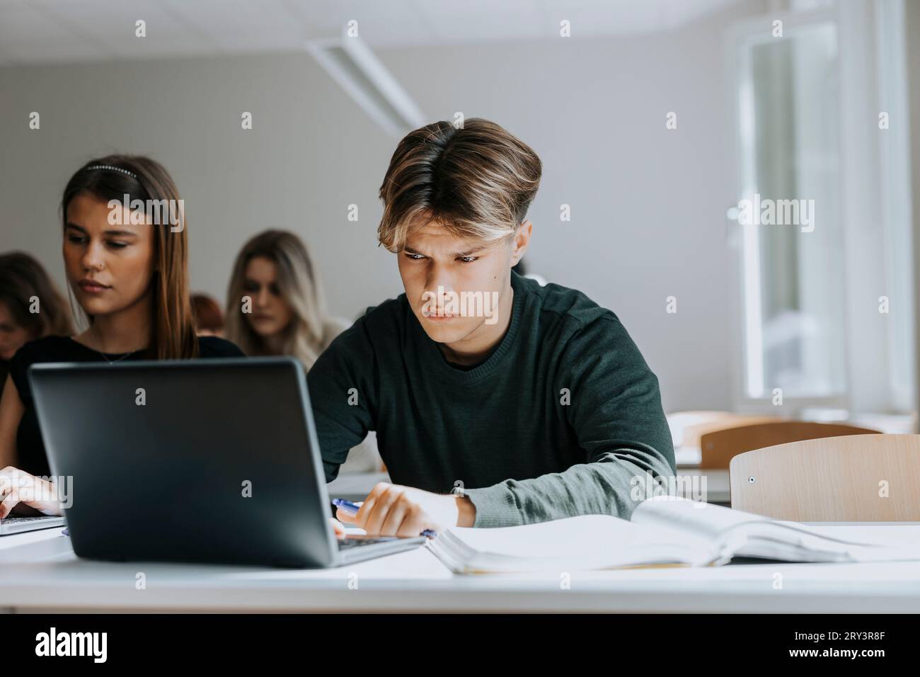 Teenage boy staring at laptop while sitting in classroom Stock Photo ...