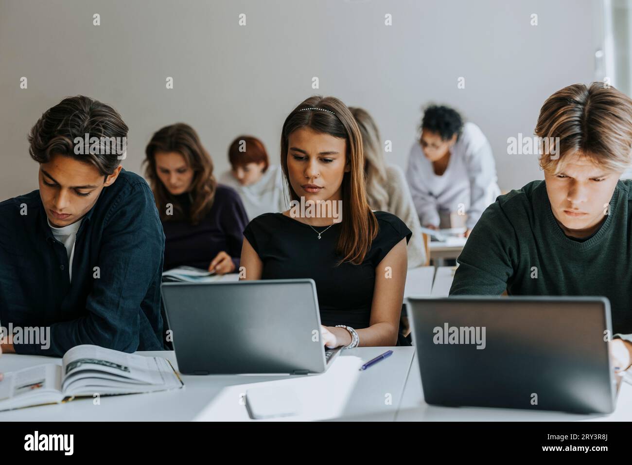 Multiracial teenage students studying at desk in classroom Stock Photo ...