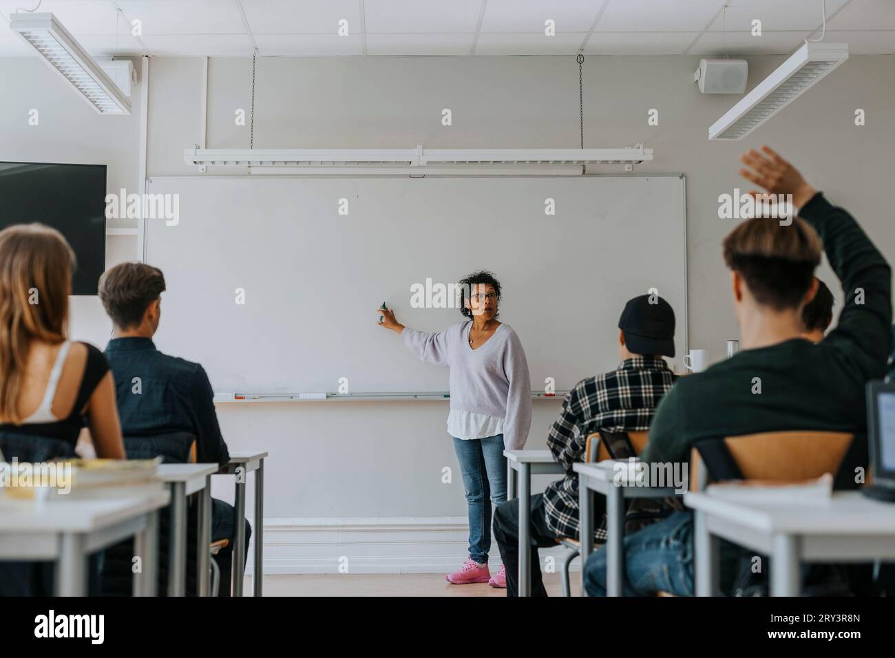 Mature female teacher pointing at whiteboard while teaching students in ...