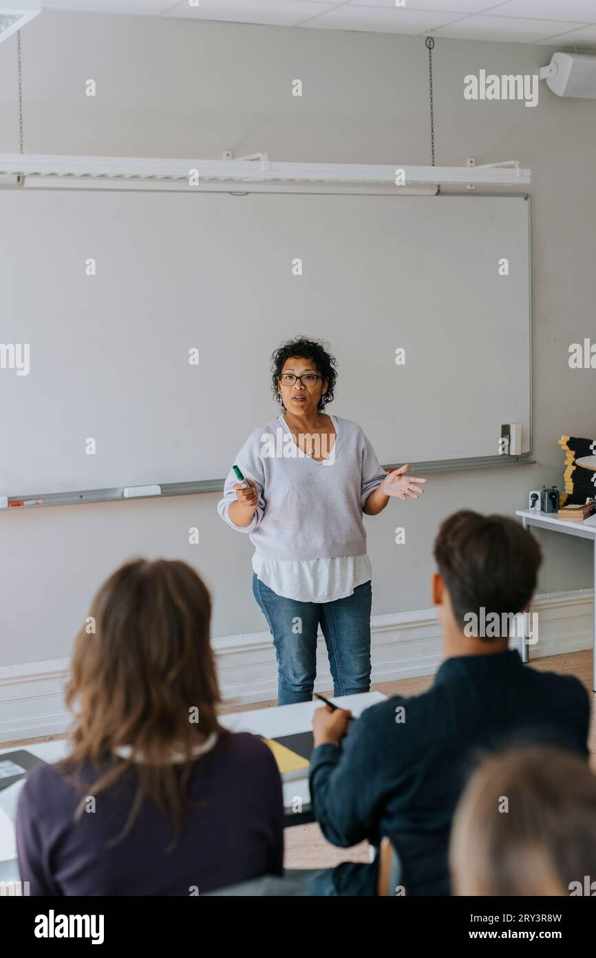Teacher gesturing while teaching students sitting in classroom Stock ...