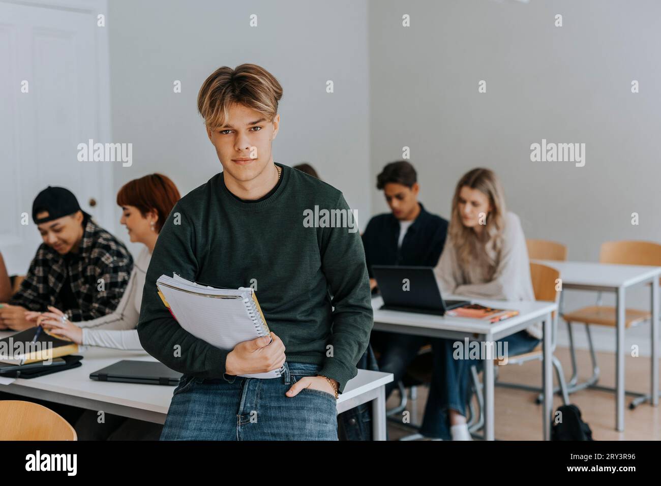 Portrait of teenage boy with book leaning on desk in classroom Stock ...