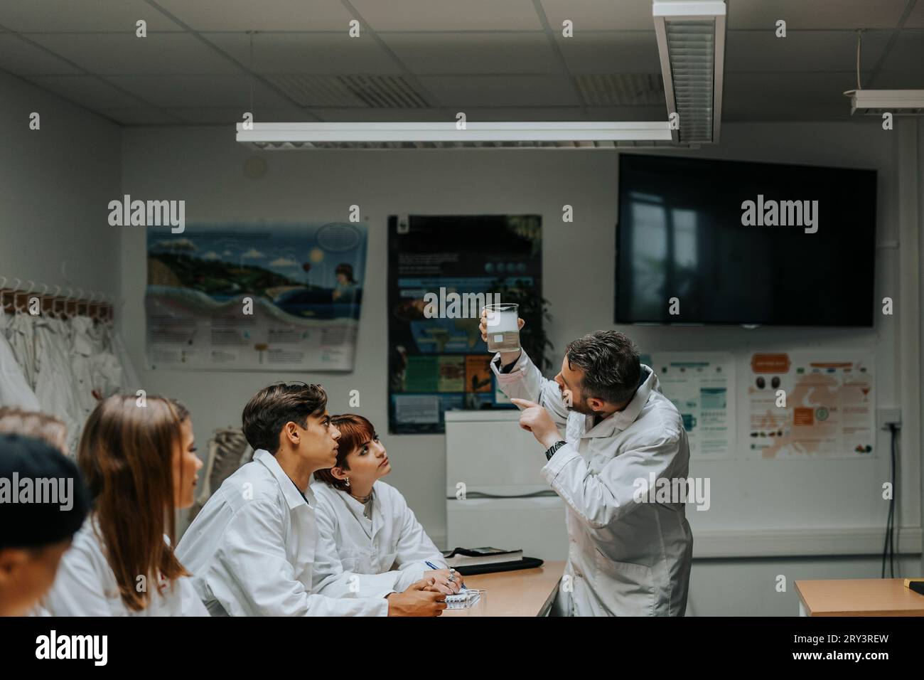Male professor examining chemical in beaker while explaining to student ...
