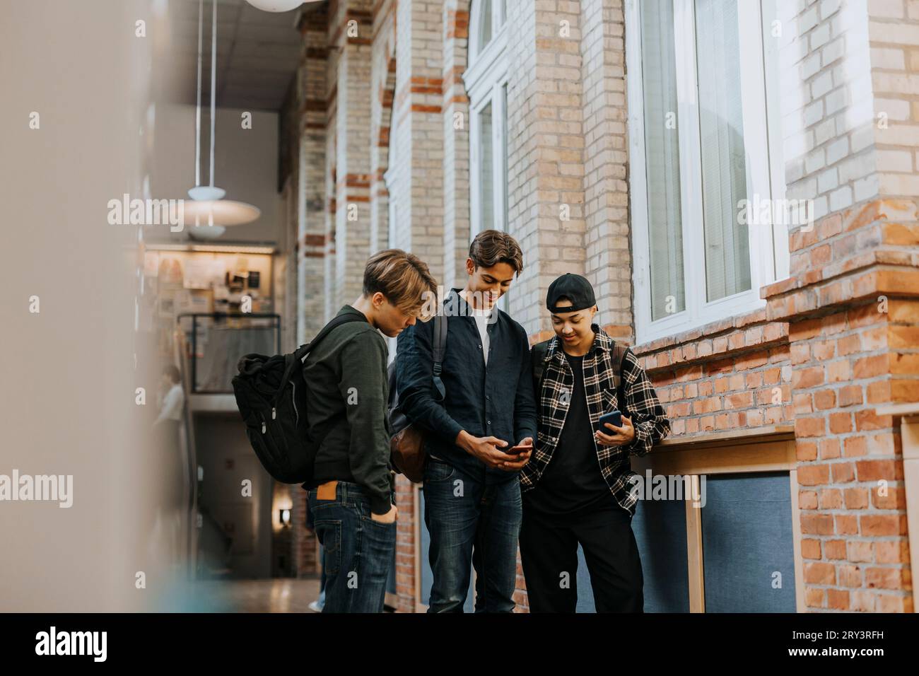 Teenage boy sharing mobile phone with friends while walking in school ...