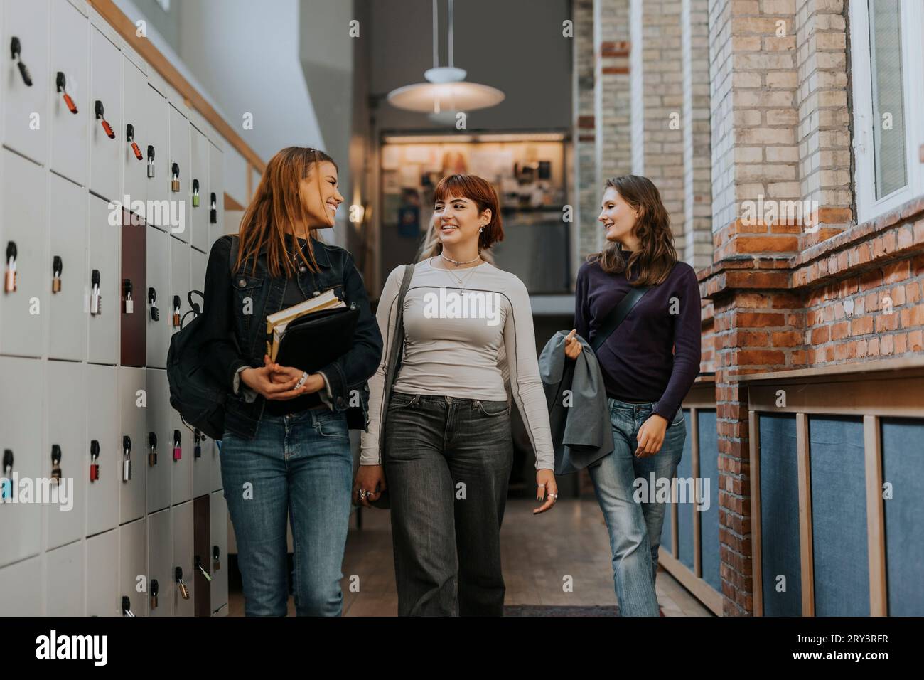 Happy female friends walking together by locker in corridor Stock Photo ...