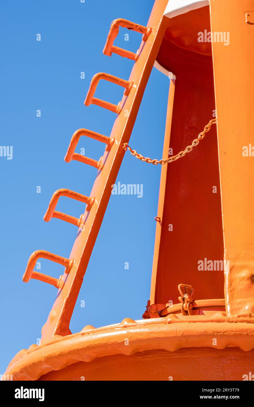 A huge metal bright orange tube on the seashore. In the background, a ...