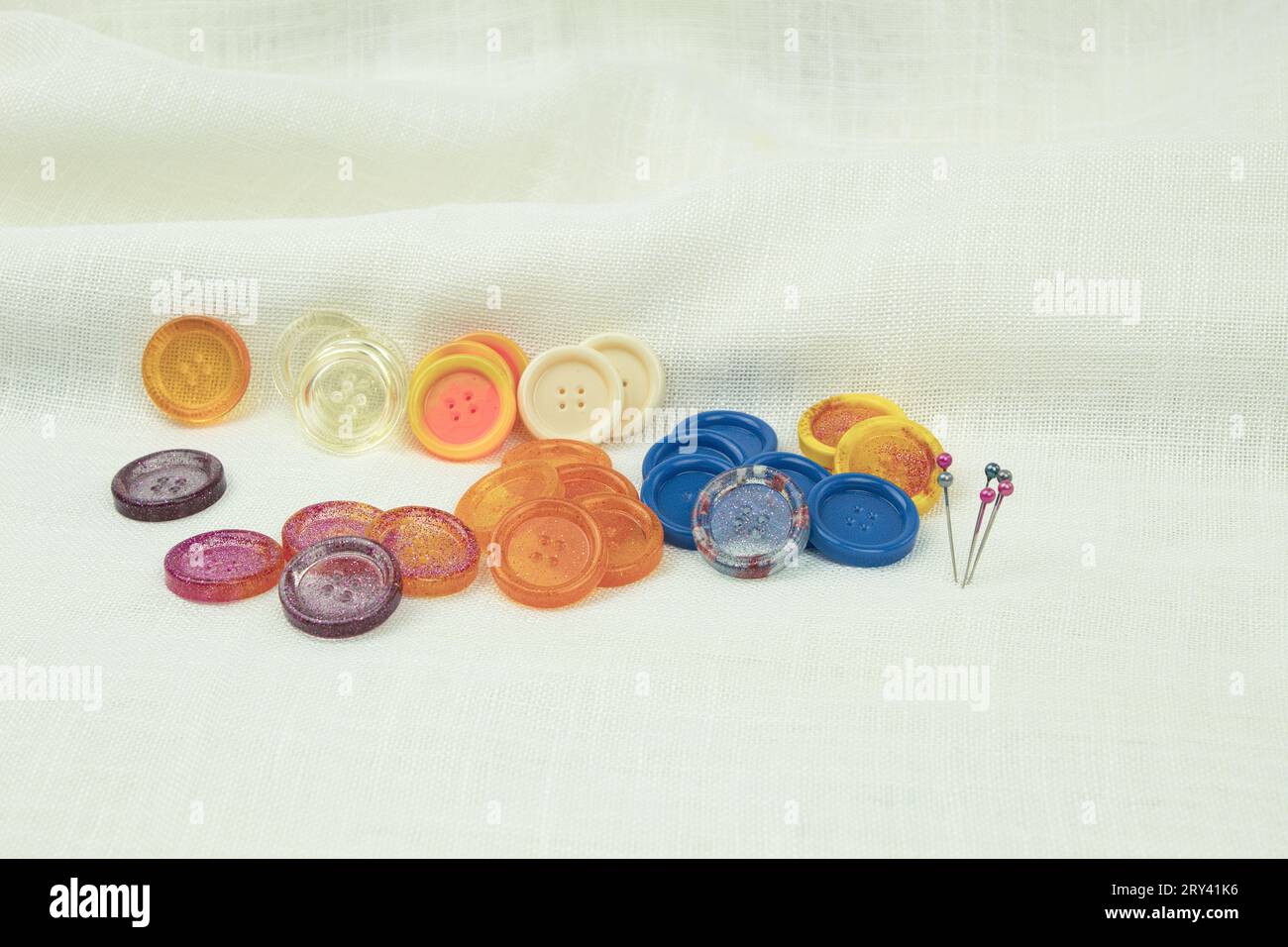 Multicolored buttons, with a needle and threads, on a fabric background ...