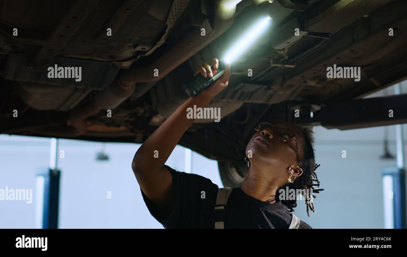 Licensed mechanic standing underneath suspended car in garage workspace ...