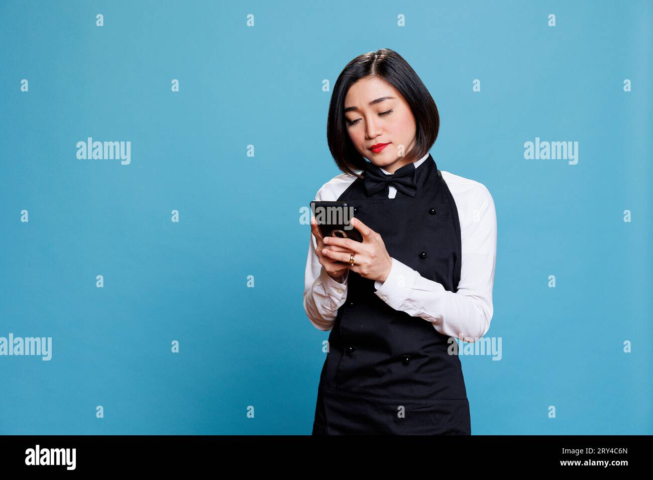 Restaurant waitress wearing uniform using smartphone to manage customer ...