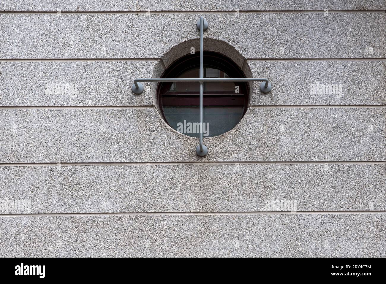 A cement wall with a porthole window with a gray painted cross grille ...