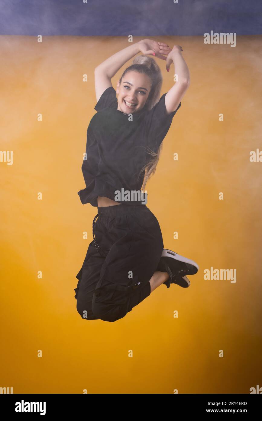 Beautiful happy girl in black outfit jumping against dark yellow or ...