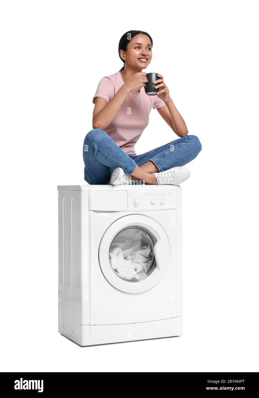 Beautiful woman with cup of drink sitting on washing machine against ...
