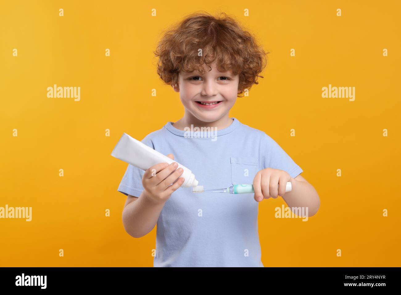 Cute little boy squeezing toothpaste from tube onto electric toothbrush ...