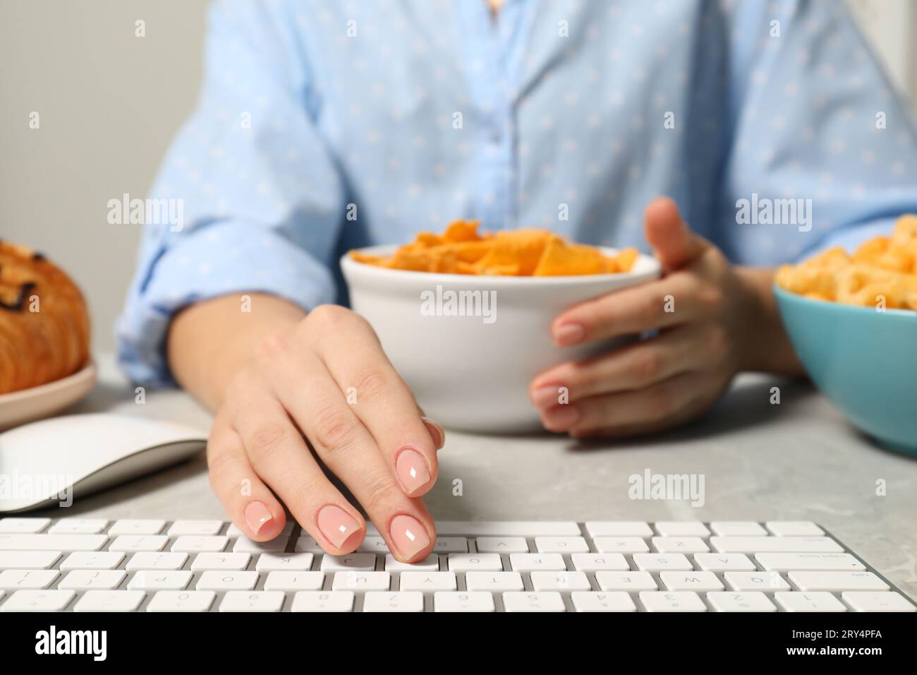 Bad eating habits. Woman working on computer at light grey table with ...