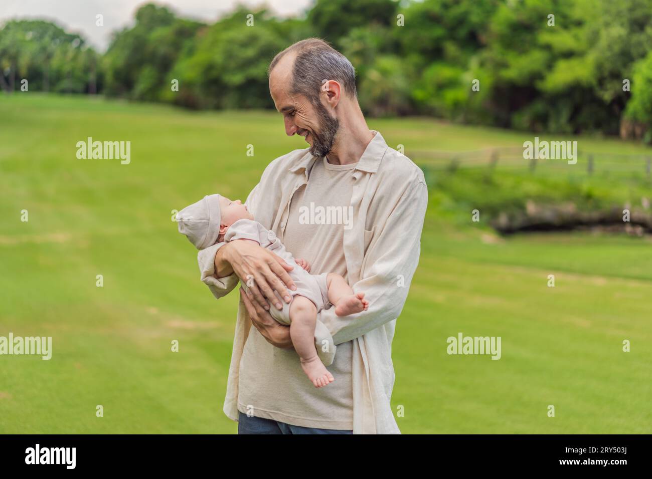 A happy 40-year-old father cradles her newborn in a sun-drenched park ...