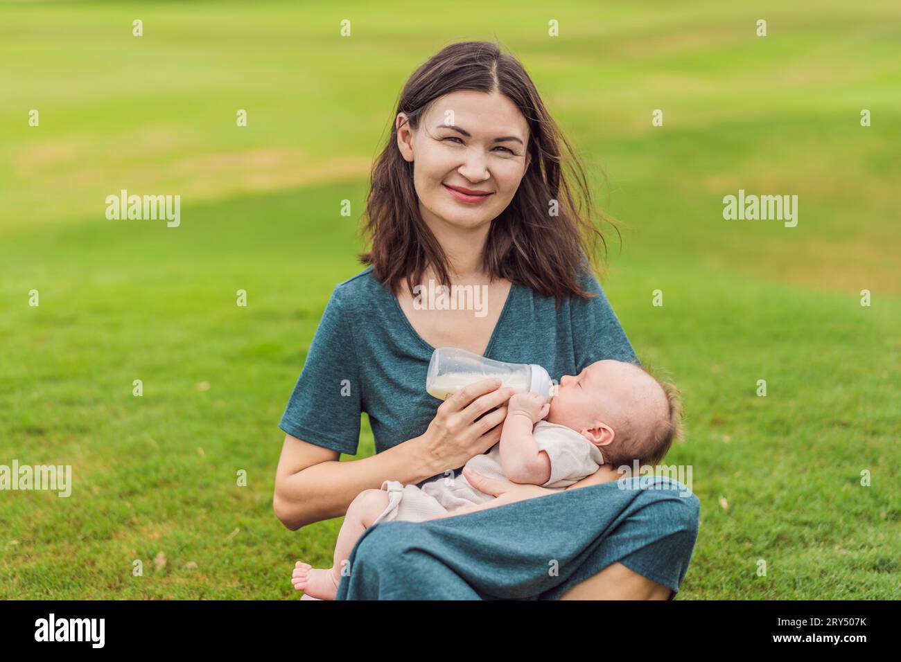 Mother holding and feeding baby from milk bottle in the park. Portrait ...