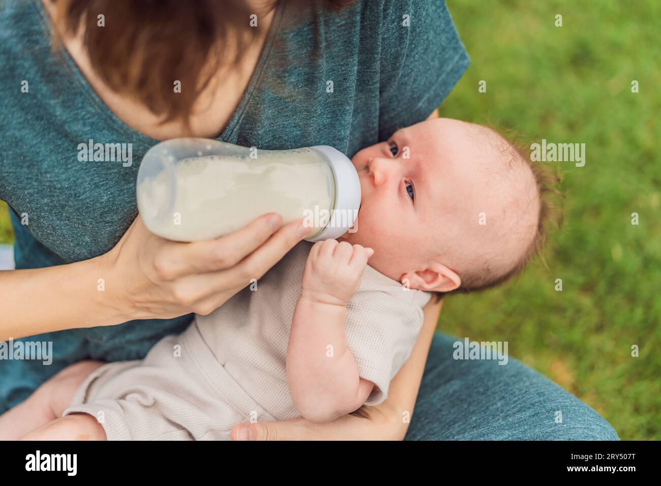 Mother holding and feeding baby from milk bottle in the park. Portrait ...