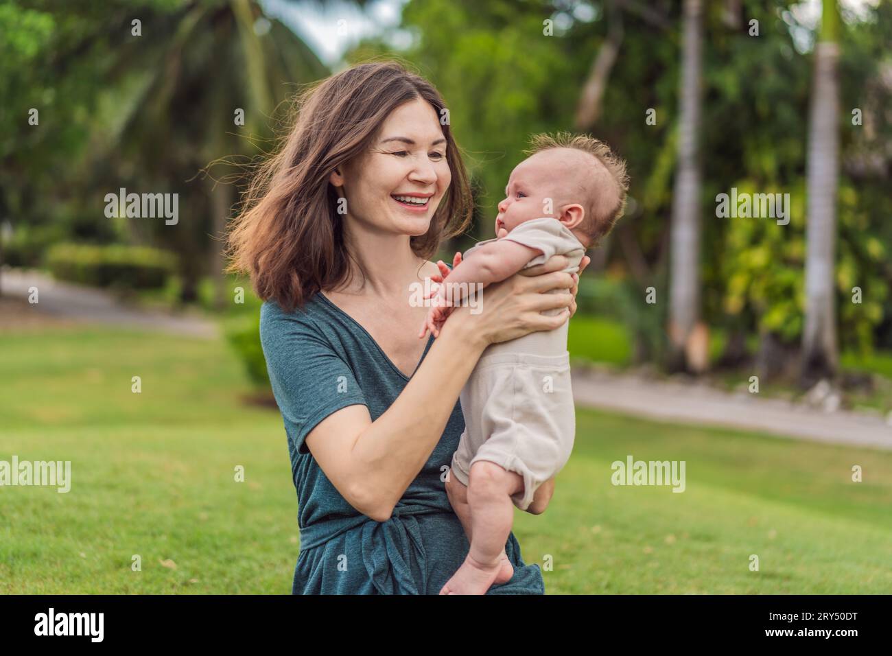 A happy 40-year-old mother cradles her newborn in a sun-drenched park ...