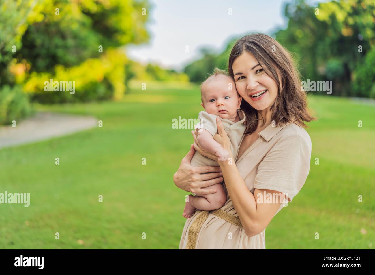 A happy 40-year-old mother cradles her newborn in a sun-drenched park ...