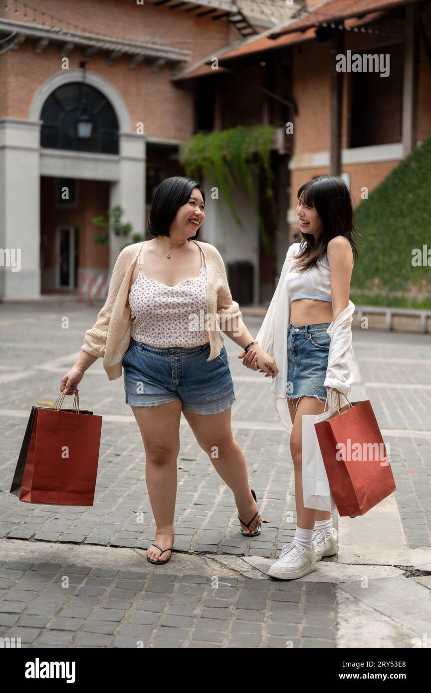 Two happy and pretty young Asian female friends are holding their ...