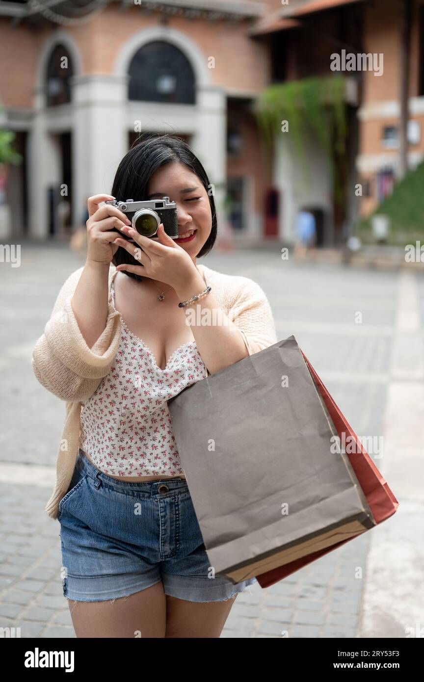 A beautiful and happy Asian plus-size woman is carrying her shopping ...