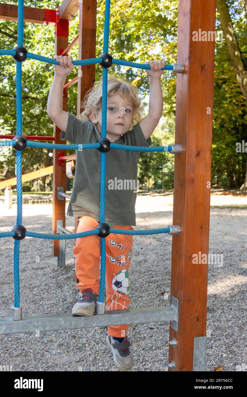 A little boy climbs on a climbing net in a children's playground Stock ...