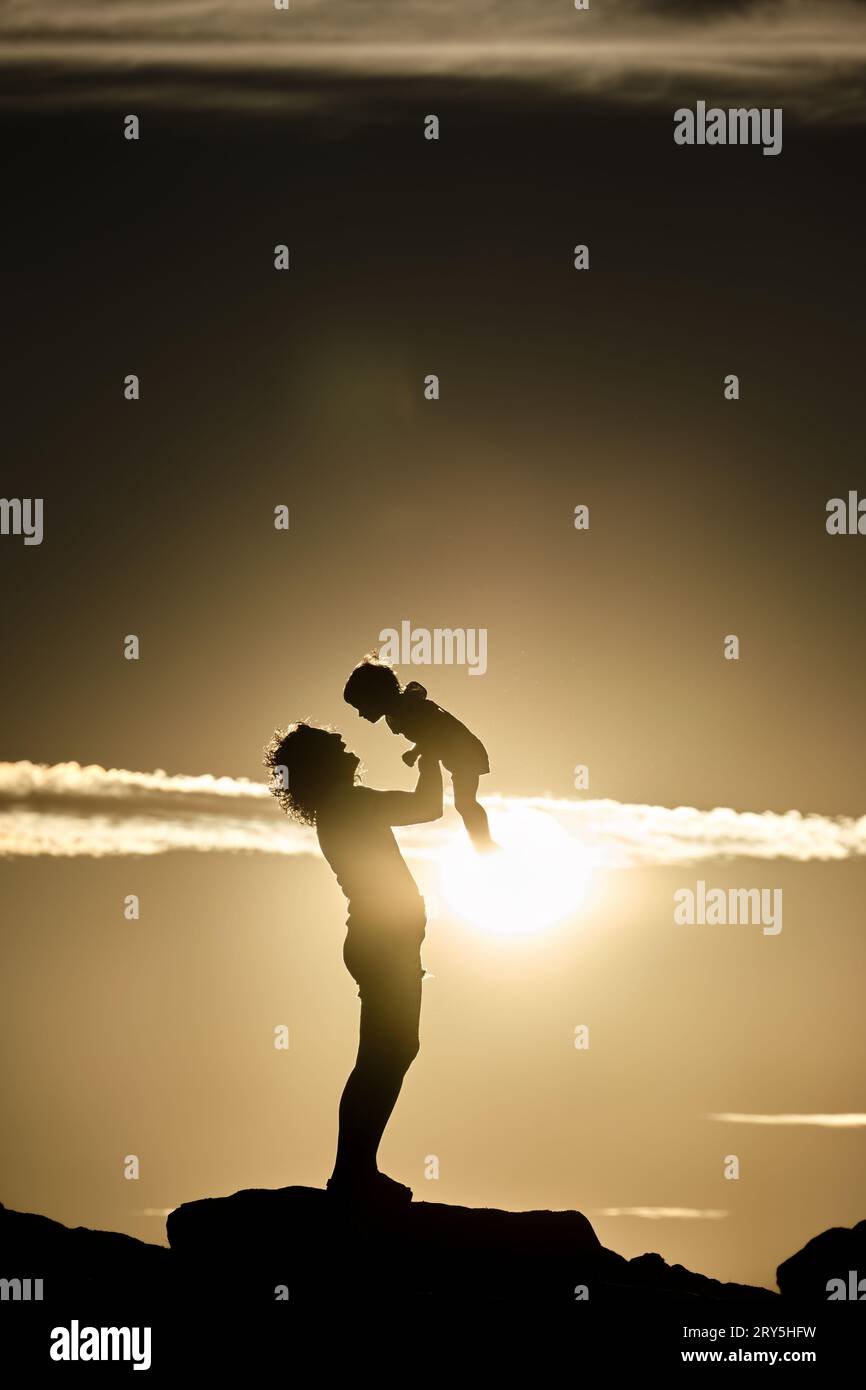 Mother lifts her son in a beautiful sunset so he can enjoy the ...