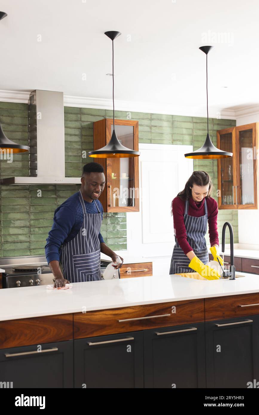Happy diverse couple cleaning countertop and doing dishes in kitchen at ...