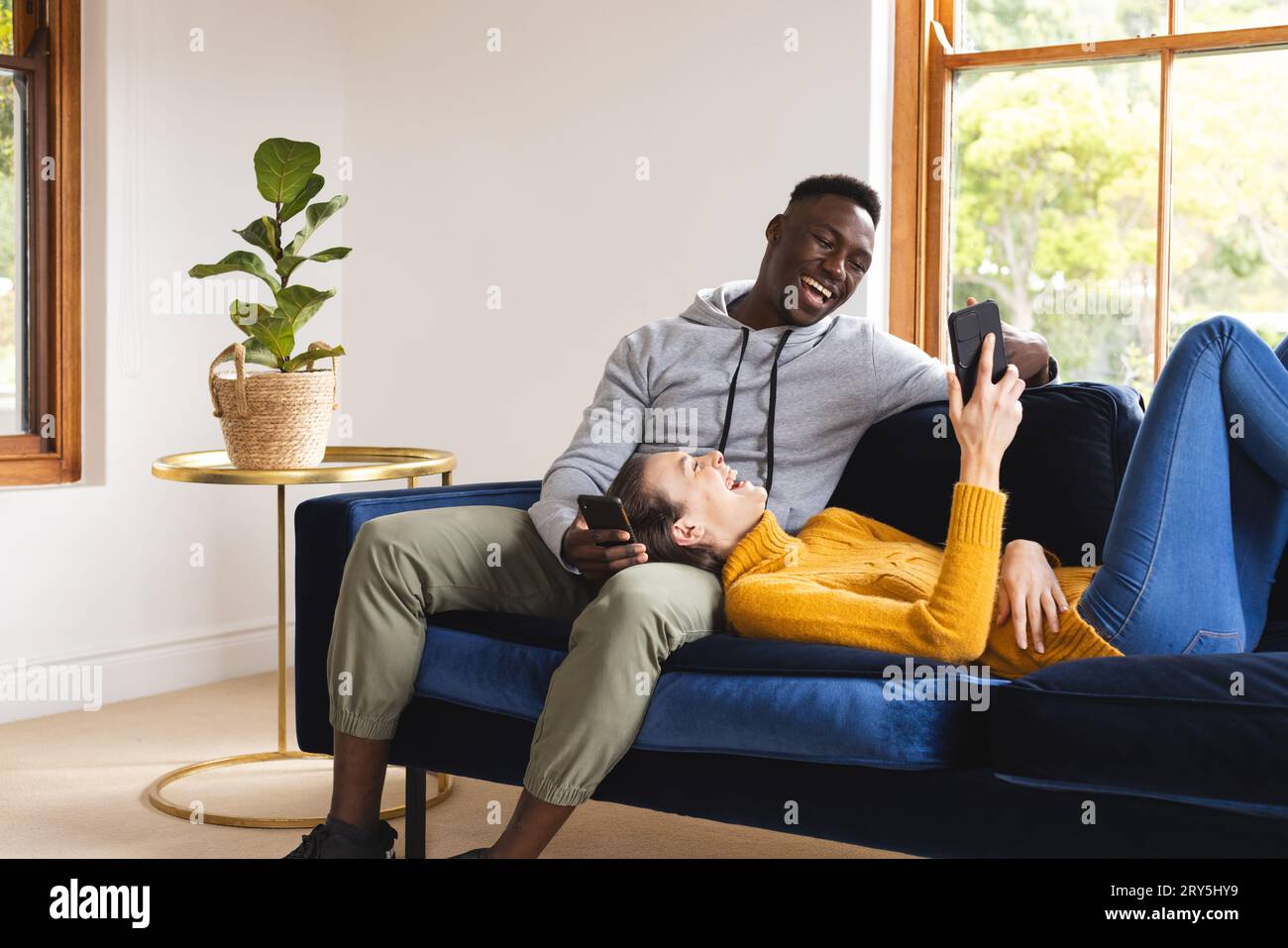 Happy diverse couple sitting on sofa using smartphones at home Stock ...