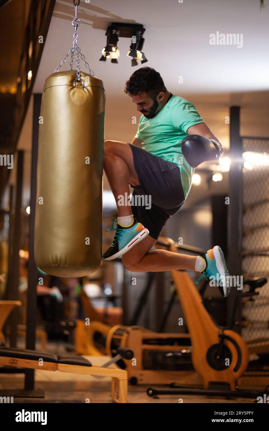 Muscular man with boxing gloves jump hitting a punching bag with a knee ...