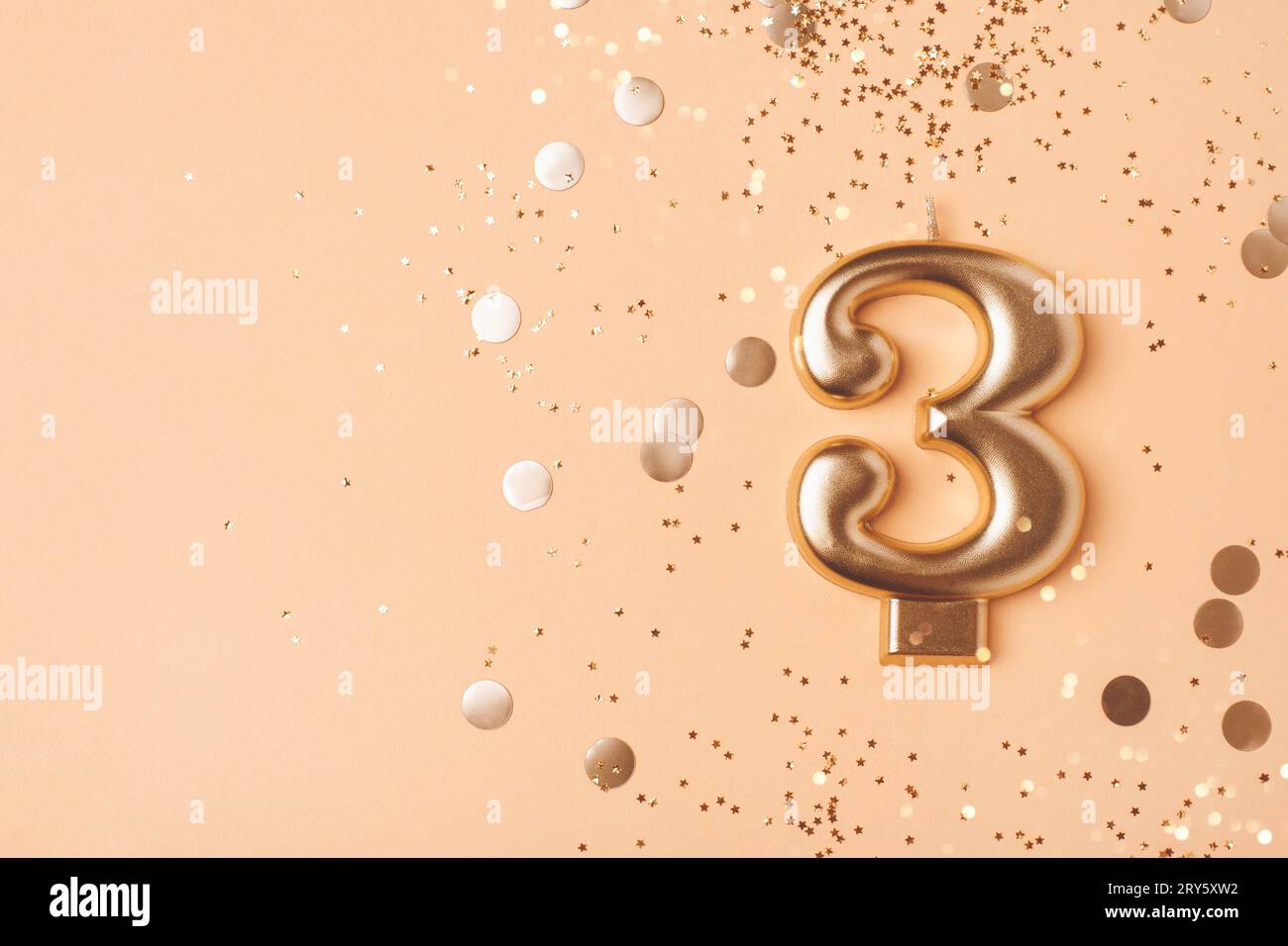 Gold candle in the form of number three on peach background with ...